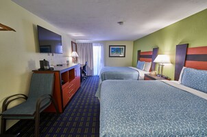 Quarto de hotel com duas camas, uma escrivaninha com cadeira, uma televisão e um quadro na parede.