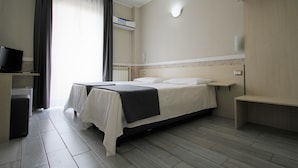 Quarto de hotel com cama, escrivaninha e televisão.