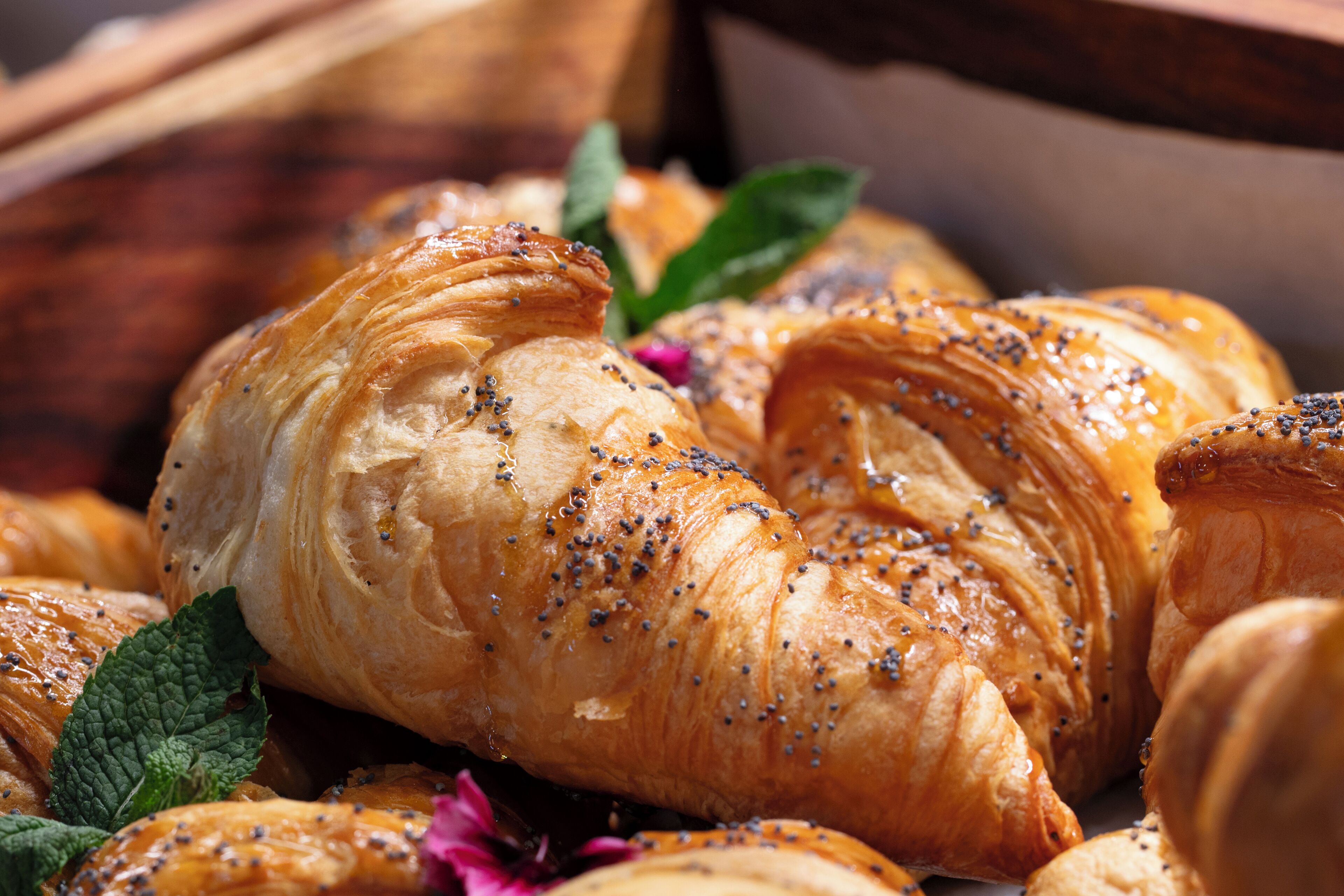 Diversos pastéis, incluindo croissants e outras iguarias assadas, decorados com folhas de hortelã e possivelmente algumas flores comestíveis.