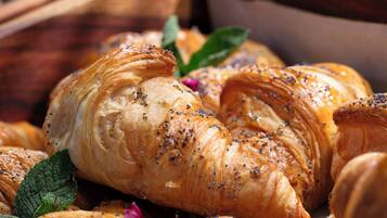 Diversos pastéis, incluindo croissants e outras iguarias assadas, decorados com folhas de hortelã e possivelmente algumas flores comestíveis.