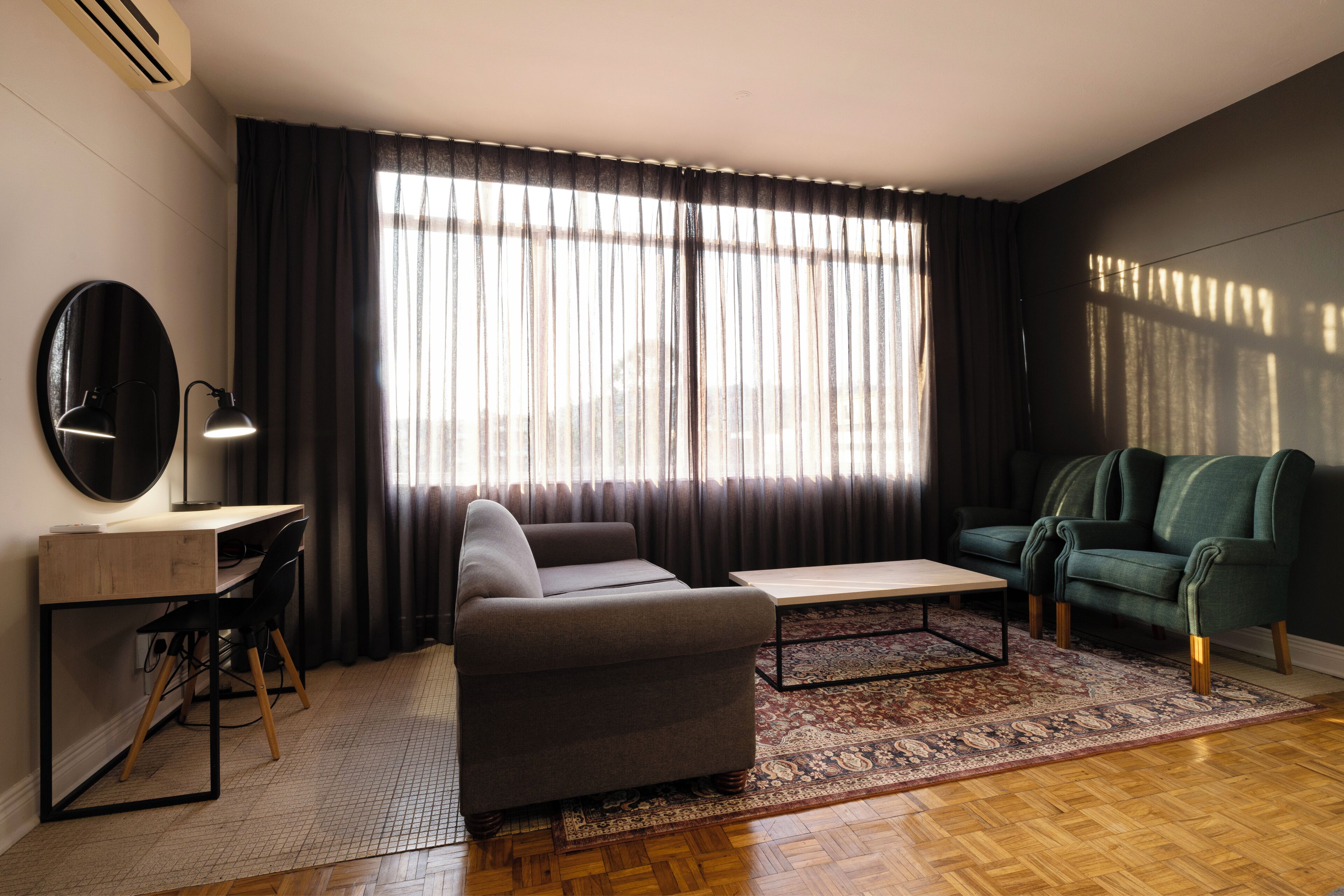 Uma sala de estar moderna com um sofá, uma mesa de centro, uma escrivaninha com uma cadeira e uma janela grande com cortinas.