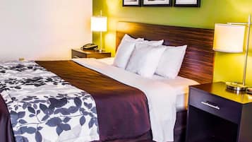 Cama bem arrumada com colcha florida, cabeceira de madeira e duas luminárias laterais.