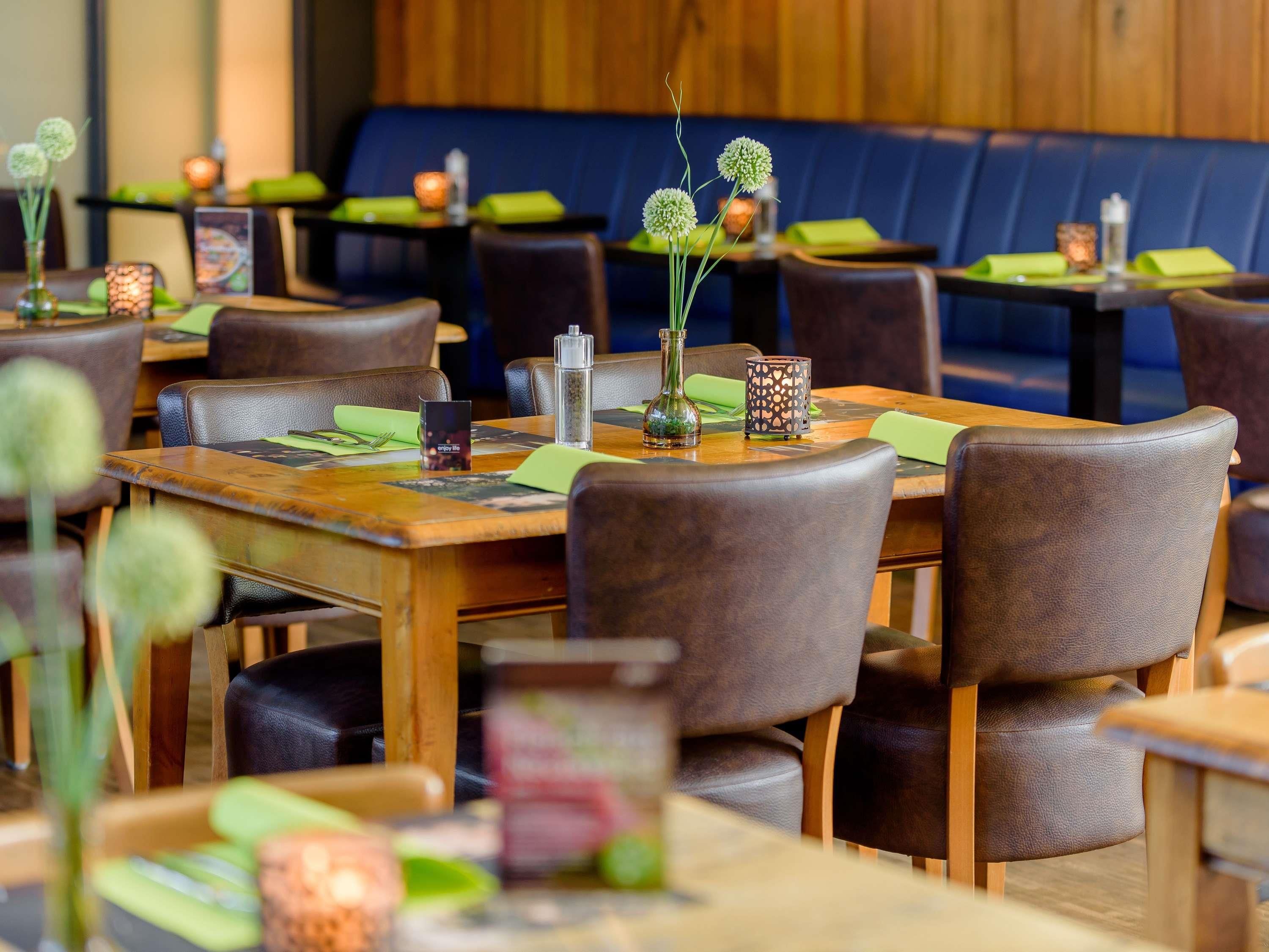 Um restaurante com mesas de madeira e cadeiras de couro, um banco acolchoado azul e vasos decorativos com flores.