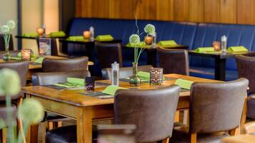 Um restaurante com mesas de madeira e cadeiras de couro, um banco acolchoado azul e vasos decorativos com flores.