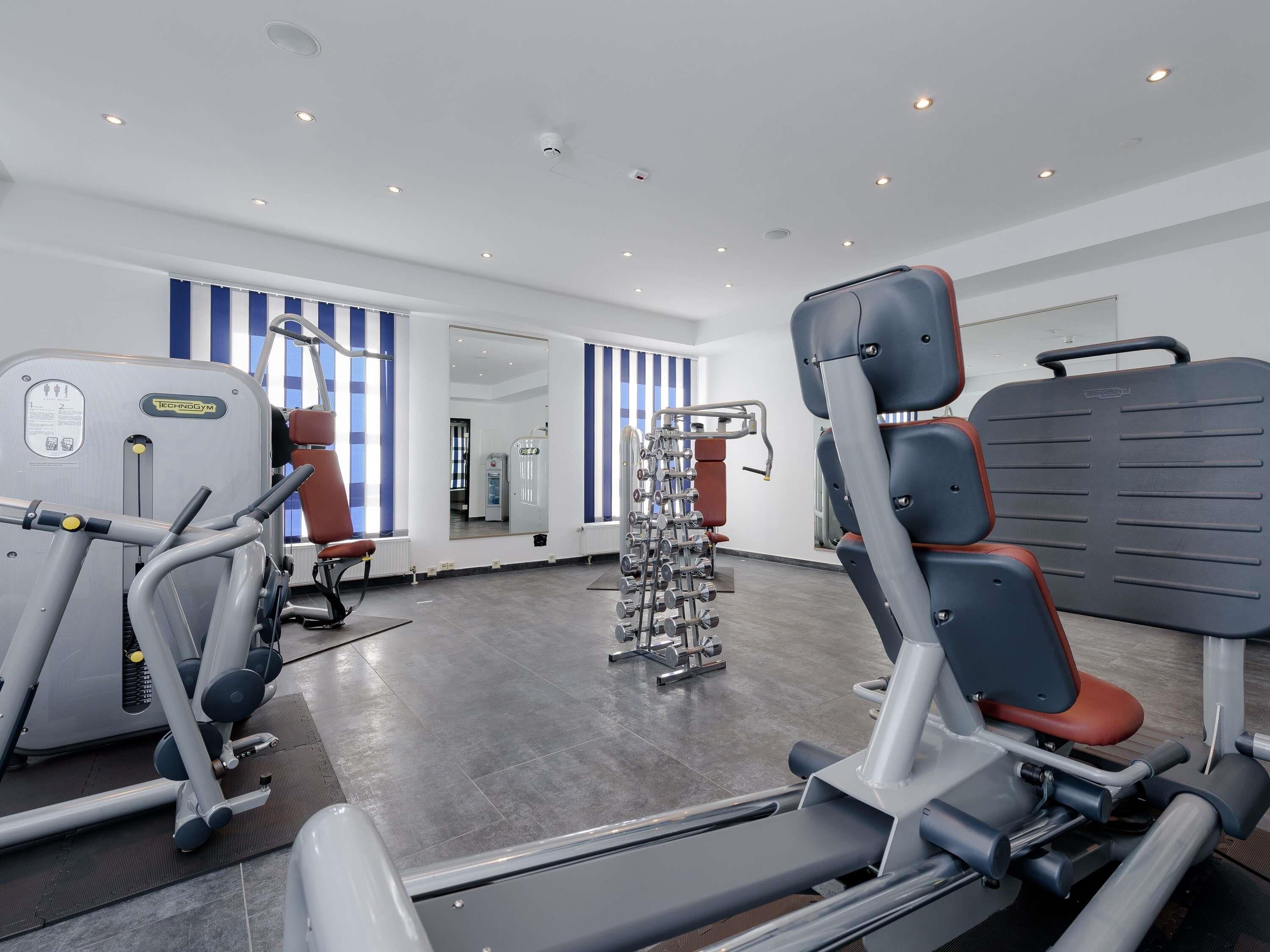 Academia com equipamentos de ginástica, um espelho e uma parede listrada em azul.