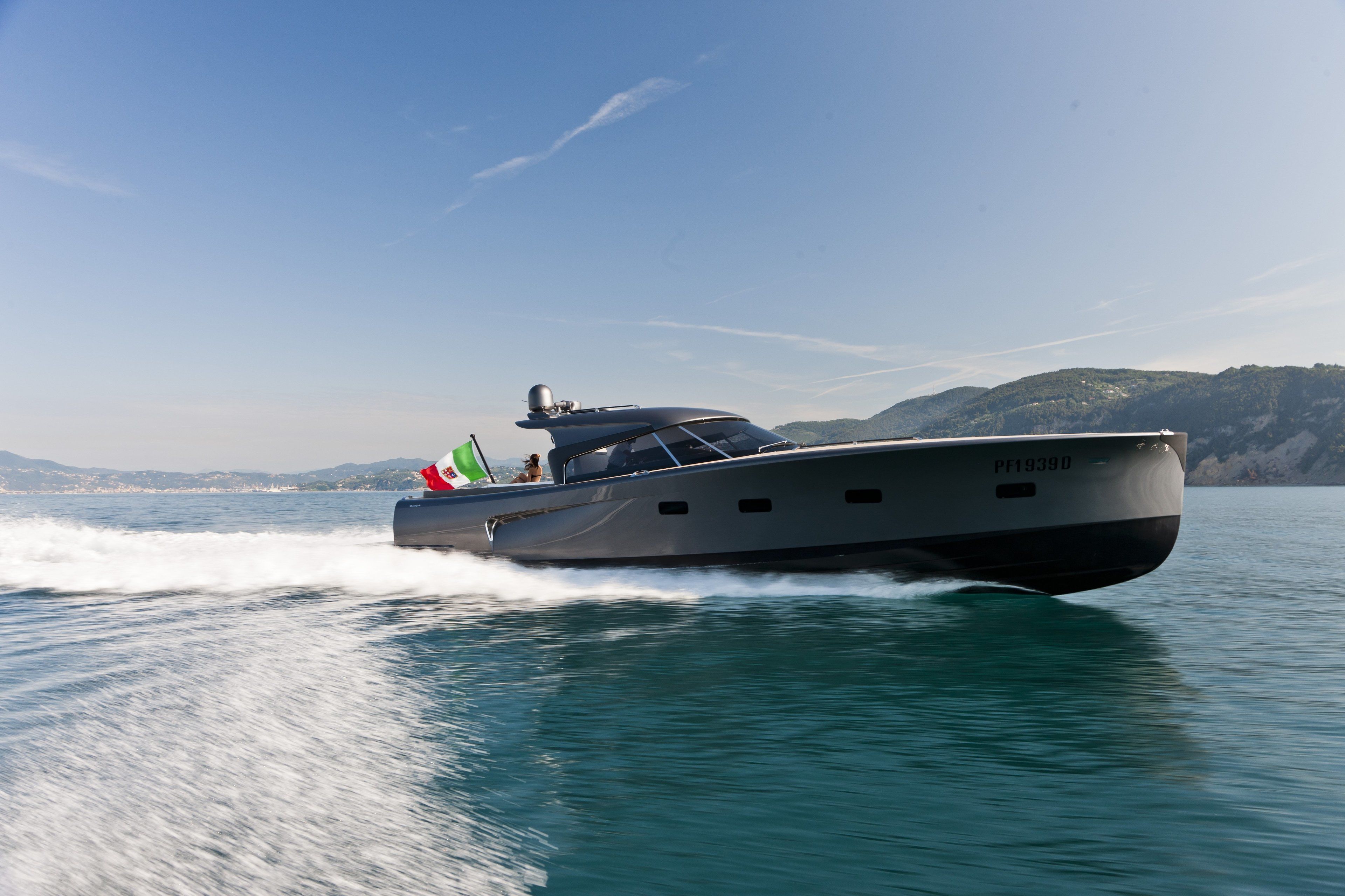 Um barco moderno e elegante, com cabine e uma bandeira verde na proa, navegando em águas calmas.