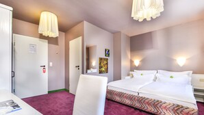 Quarto de hotel com uma cama, uma escrivaninha, uma cadeira e uma porta.
