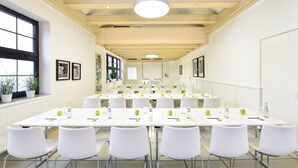 Uma sala de conferências com mesas e cadeiras brancas, plantas em vasos e uma lousa.