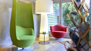 Quarto moderno com uma cadeira verde, uma cadeira vermelha, um abajur branco e uma pequena mesa com maçãs.