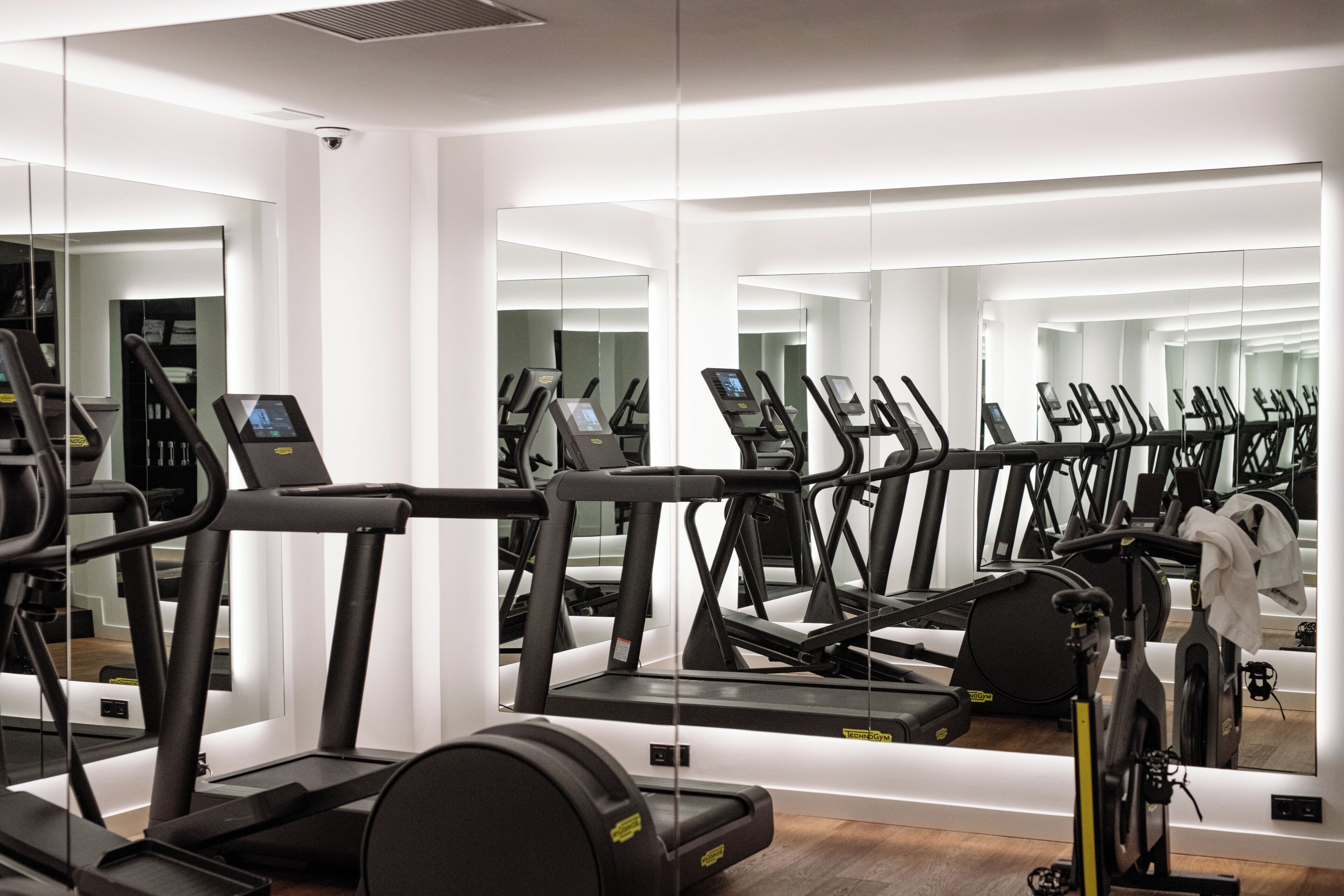 Uma academia com várias esteiras e bicicletas de exercício, paredes com espelhos e um design moderno e limpo.