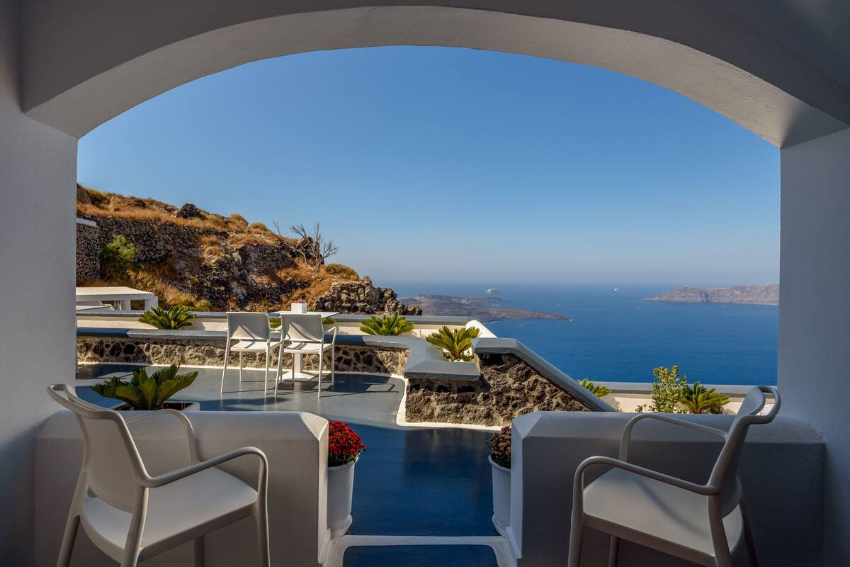 Um terraço com vista para o mar, cadeiras brancas e plantas em vasos.