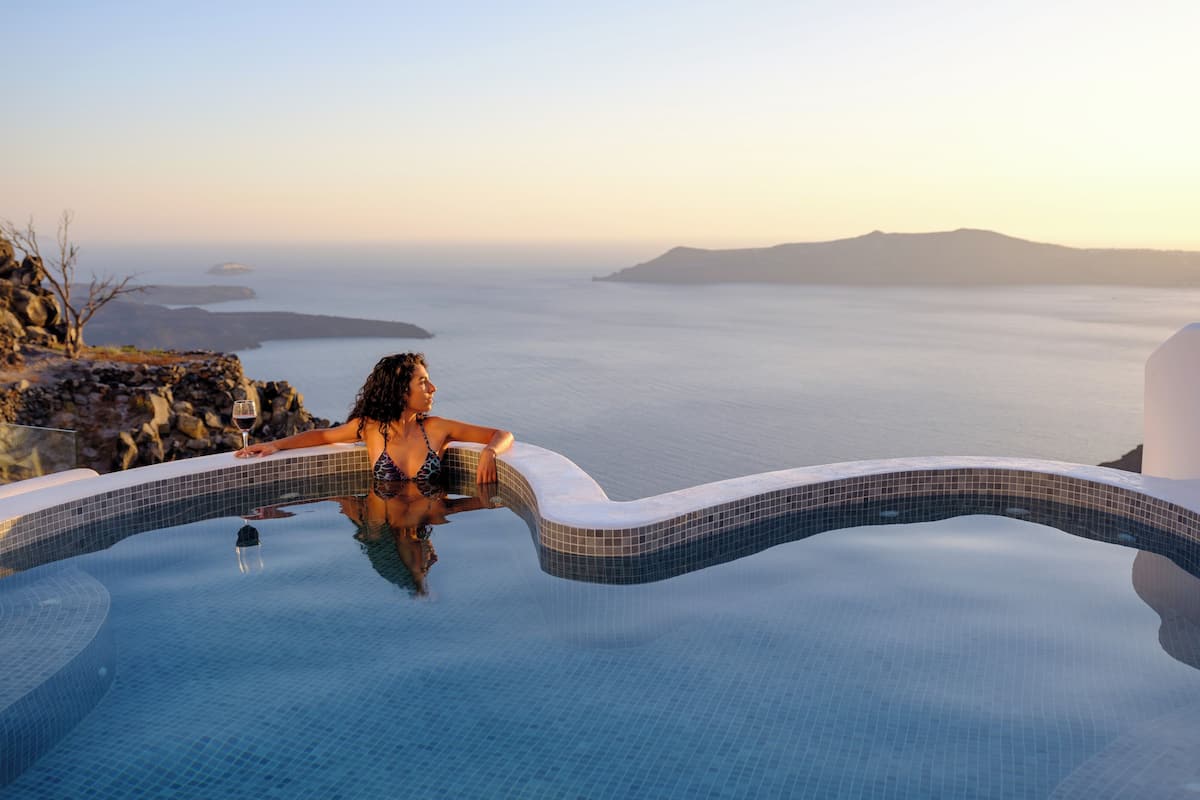 Uma pessoa relaxando em uma piscina infinita, com vista para o mar e ilhas ao longe.