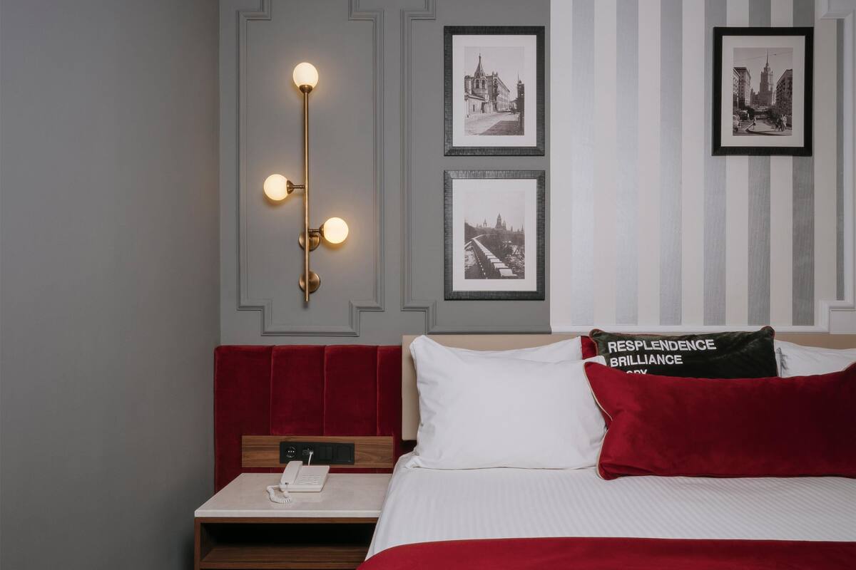 Quarto de hotel com cama, mesa de cabeceira, luminária fixada na parede e quadros emoldurados.