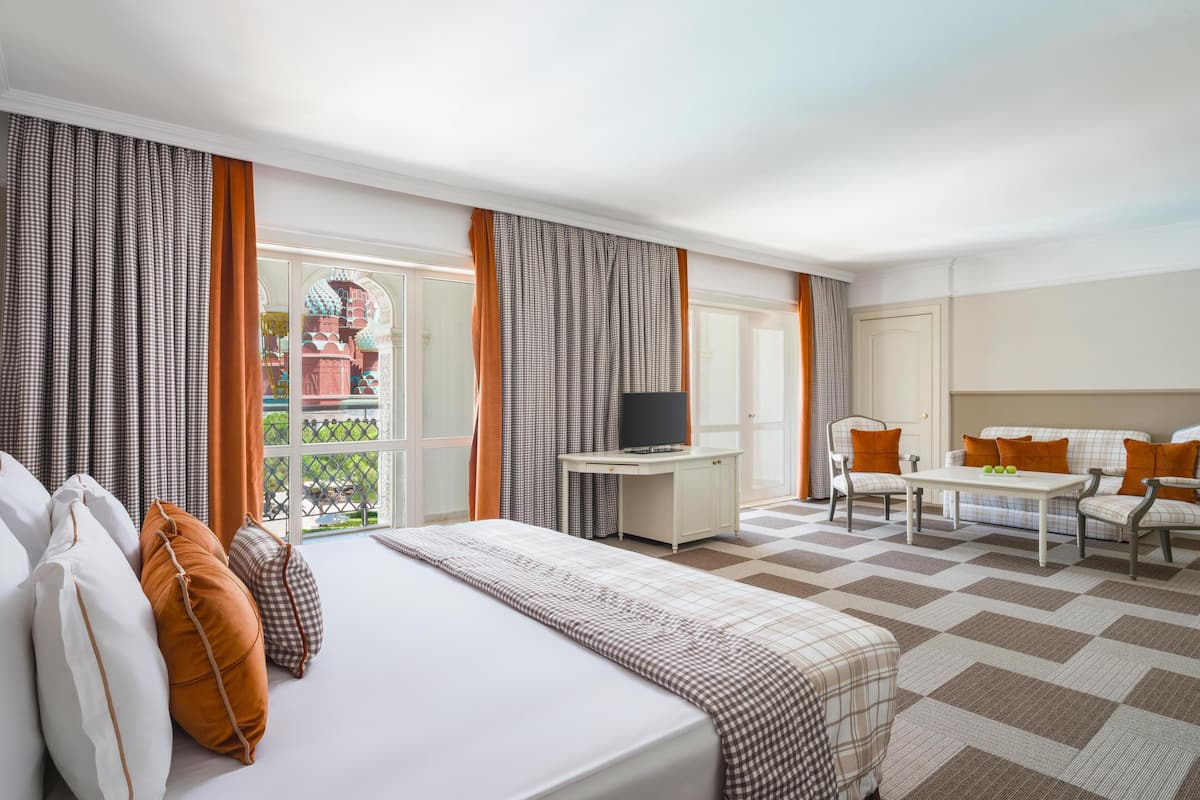Quarto de hotel com cama, escrivaninha, televisão e área de refeições com mesa e cadeiras.
