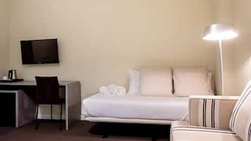 Quarto de hotel com uma cama, uma escrivaninha com cadeira, uma televisão na parede e um abajur.