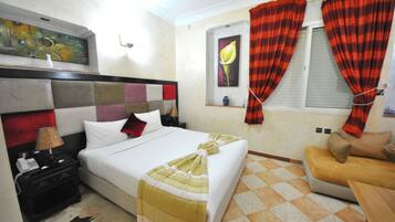 Quarto de hotel com cama, mesa de cabeceira, luminária e janela com cortinas.