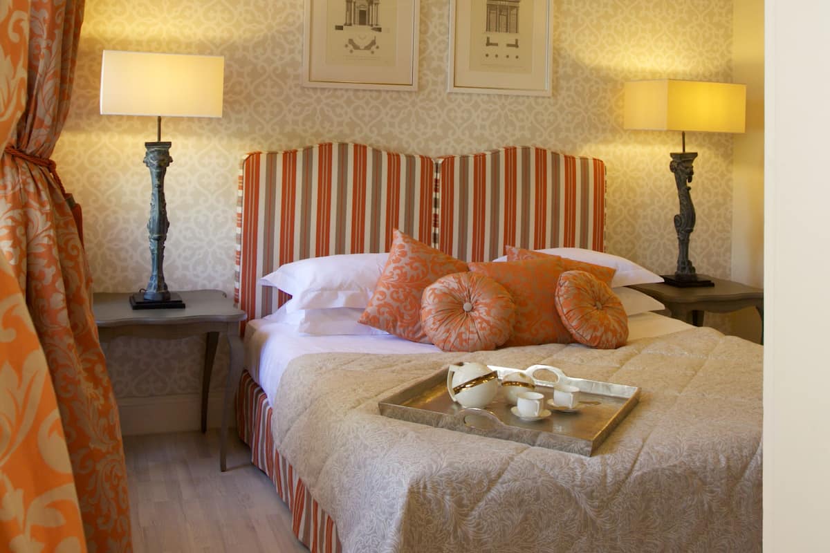 Cama bem arrumada com roupa de cama listrada, duas luminárias de cabeceira e um tabuleiro com chá.