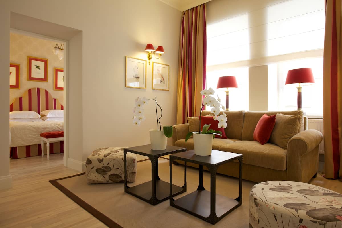 Uma sala de estar moderna com sofá, duas mesas, um banquinho e uma cama com cortinas listradas.