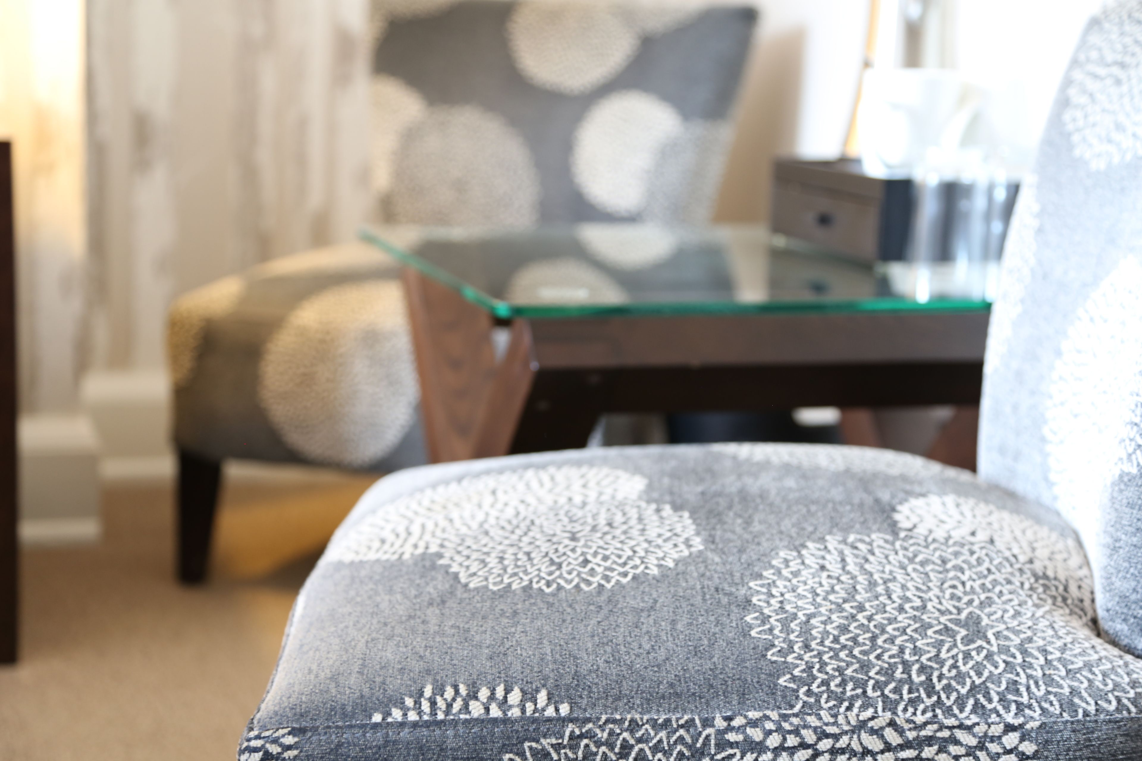Uma cadeira com estampa geométrica, uma mesa com tampo de vidro e um almofado estampado.