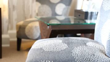 Uma cadeira com estampa geométrica, uma mesa com tampo de vidro e um almofado estampado.