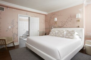 Quarto com cama grande, cadeira, mesa de cabeceira e luminária.