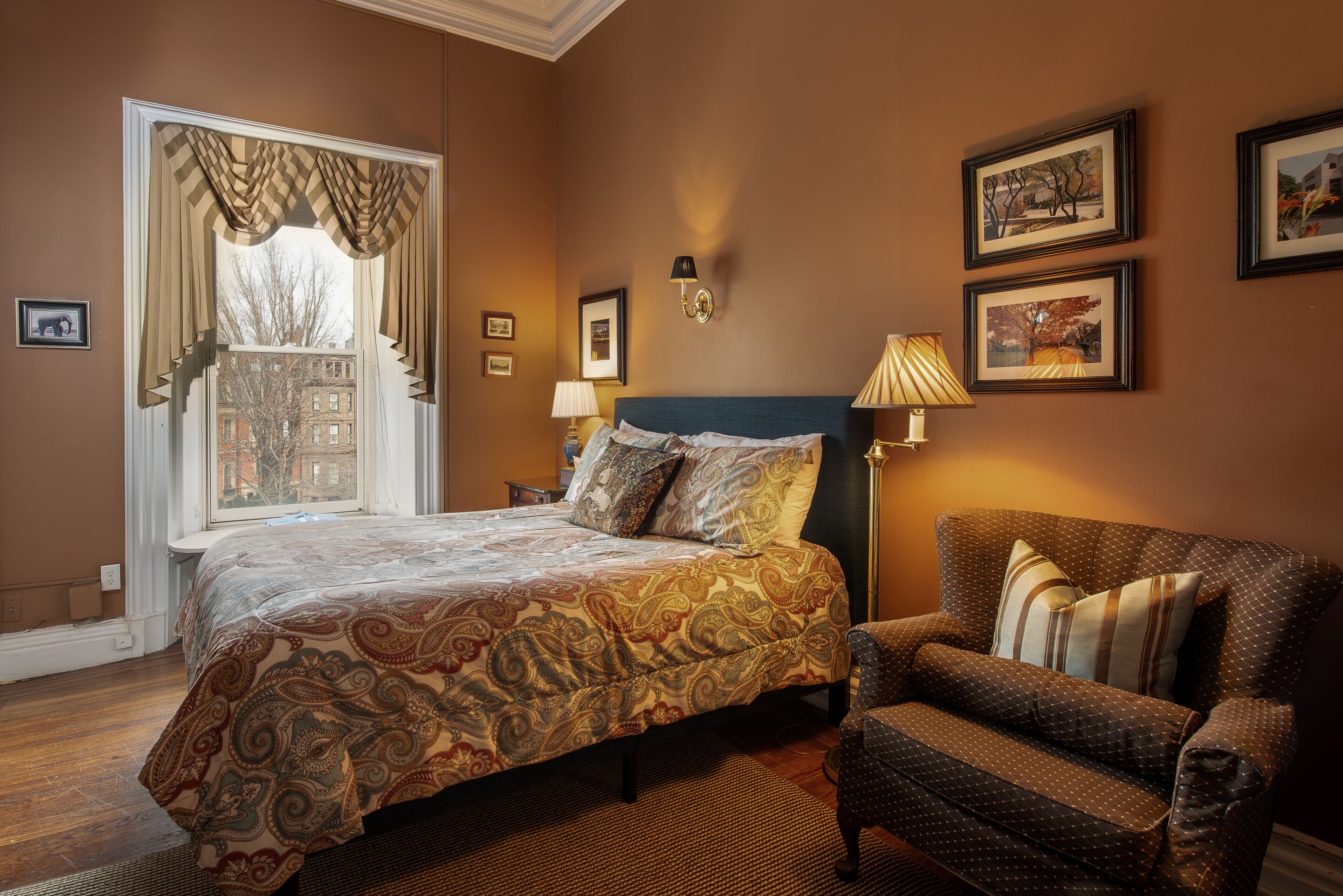 Quarto com cama grande, uma cadeira, janela com cortinas e luminárias na parede.