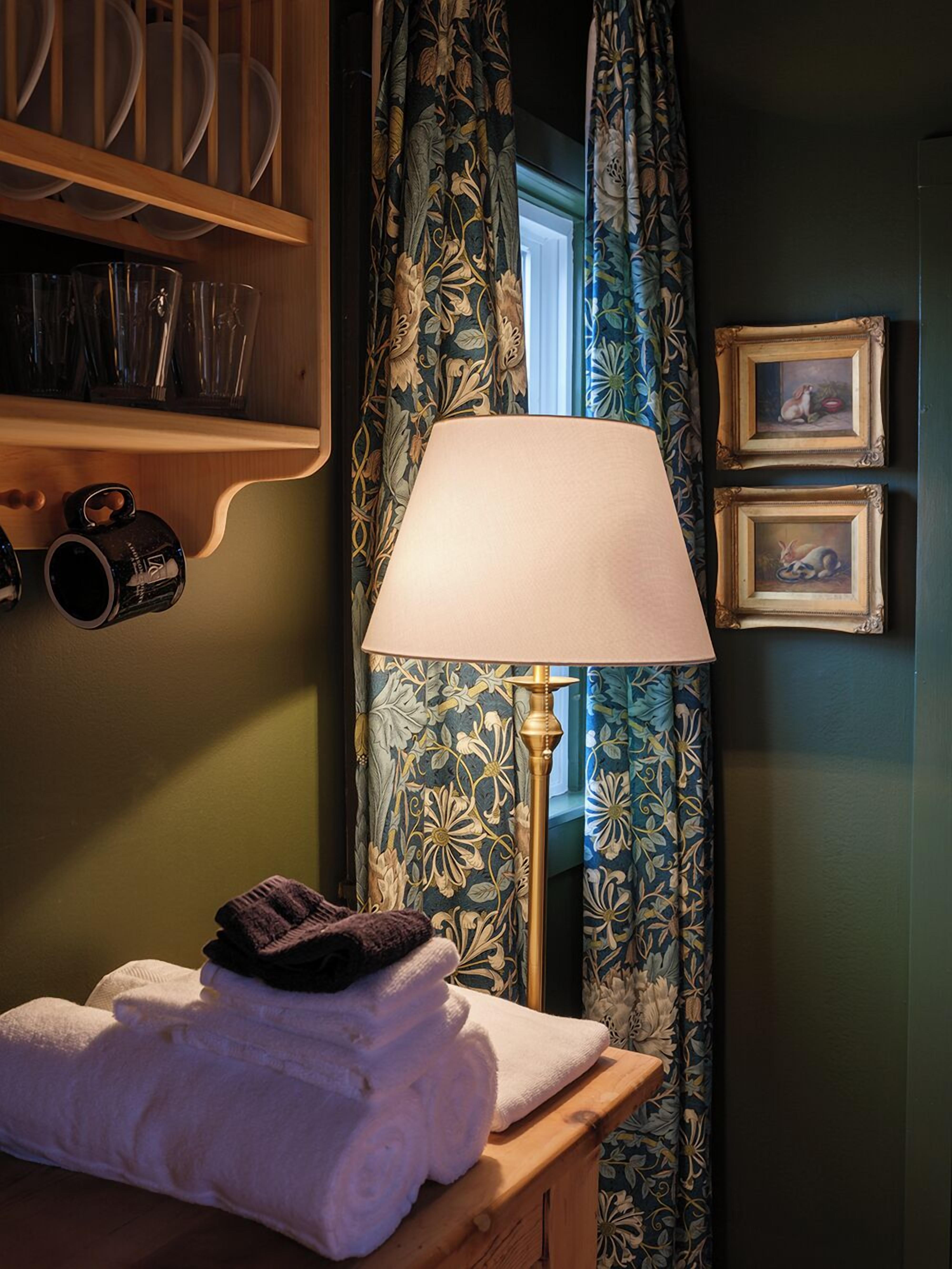 Cama bem arrumada com toalhas dobradas, uma luminária e uma estante com pratos e copos.