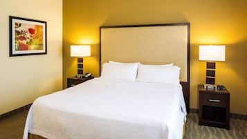 Uma cama bem arrumada com roupa de cama branca, duas mesas de cabeceira com abajures e um quadro na parede.