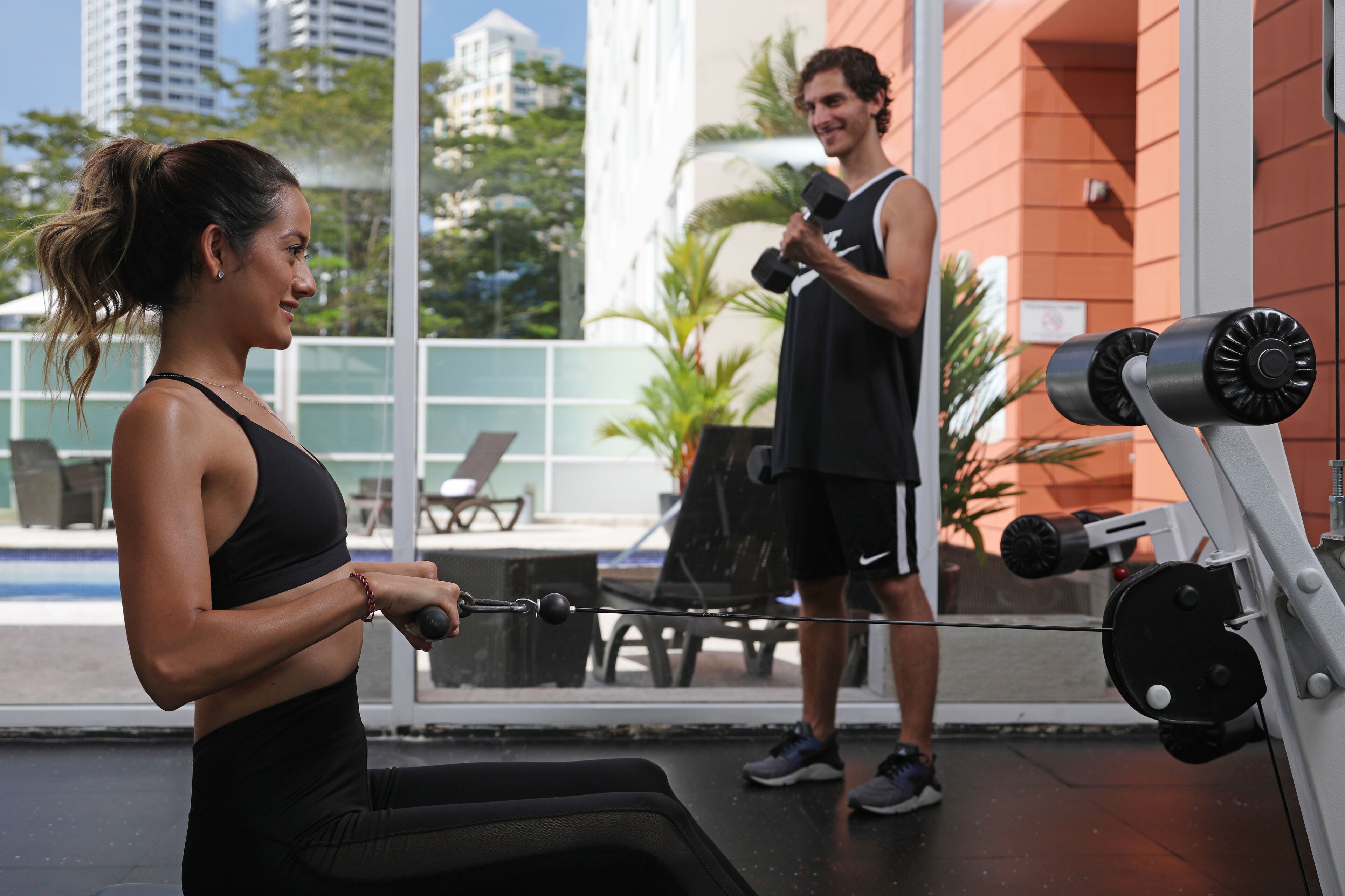 Academia com equipamentos de ginástica e uma pessoa utilizando uma máquina de cabos.