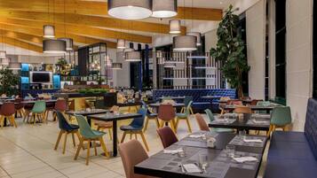 Interior moderno de restaurante com várias áreas de refeição, teto de madeira e luminárias contemporâneas.
