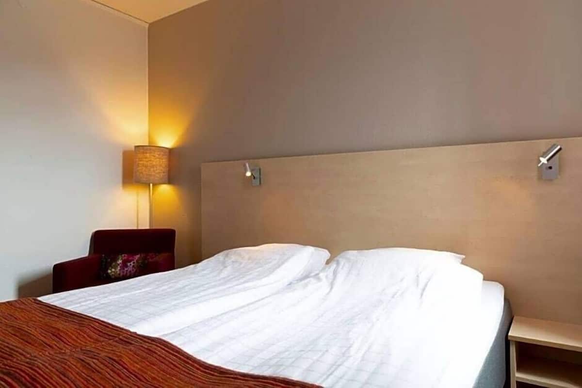 Quarto de hotel com uma cama grande, uma cadeira e um abajur.
