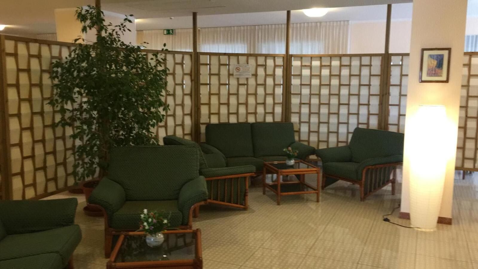 Quarto com cadeiras estofadas em verde, uma mesa pequena e uma planta em vaso.