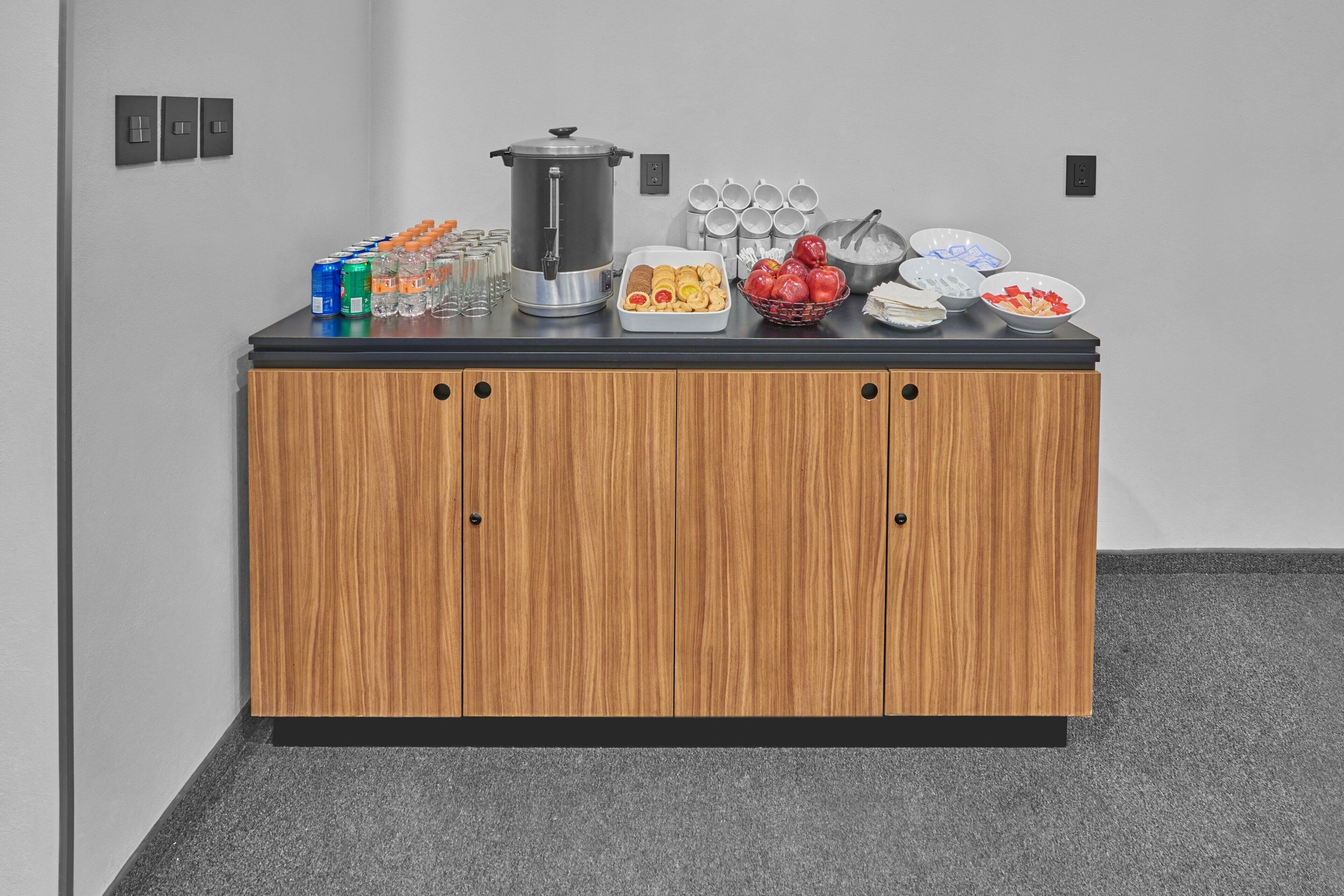 Disposição de buffet com cafeteira, bebidas e diversos alimentos sobre um balcão de madeira.