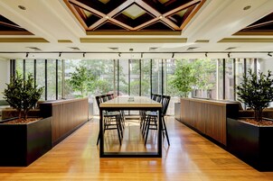 Uma sala de conferências moderna com uma mesa comprida, cadeiras pretas e piso de madeira.
