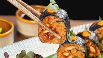 Sushis com pauzinhos, decorados com folhas e fatias de laranja, sobre um prato com folha verde embaixo.