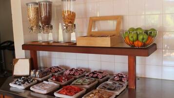 Buffet montado com diversos alimentos e uma cesta de frutas.