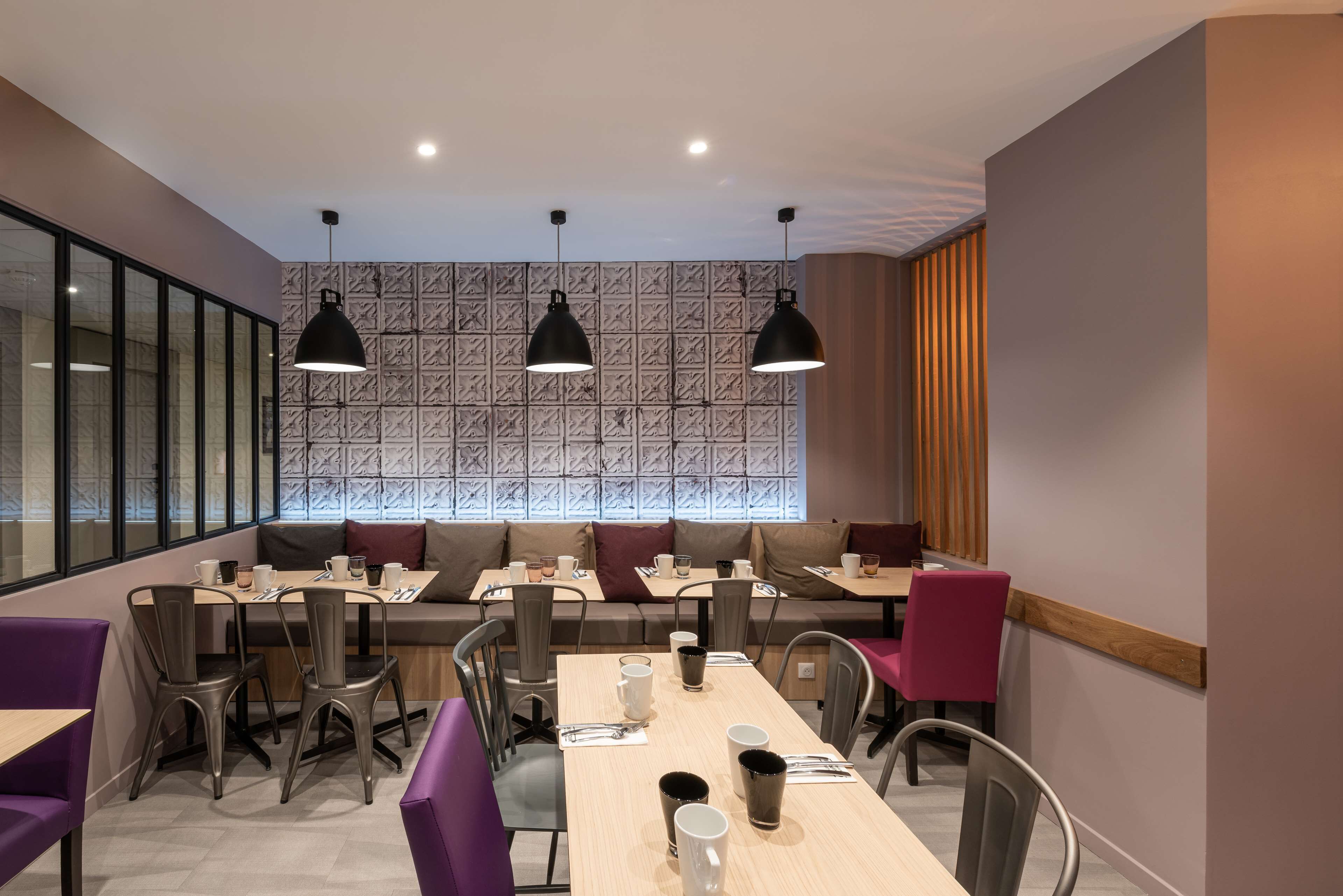 Uma sala de jantar moderna com várias mesas e cadeiras, parede estampada e luminárias pendentes.