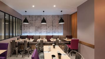 Uma sala de jantar moderna com várias mesas e cadeiras, parede estampada e luminárias pendentes.