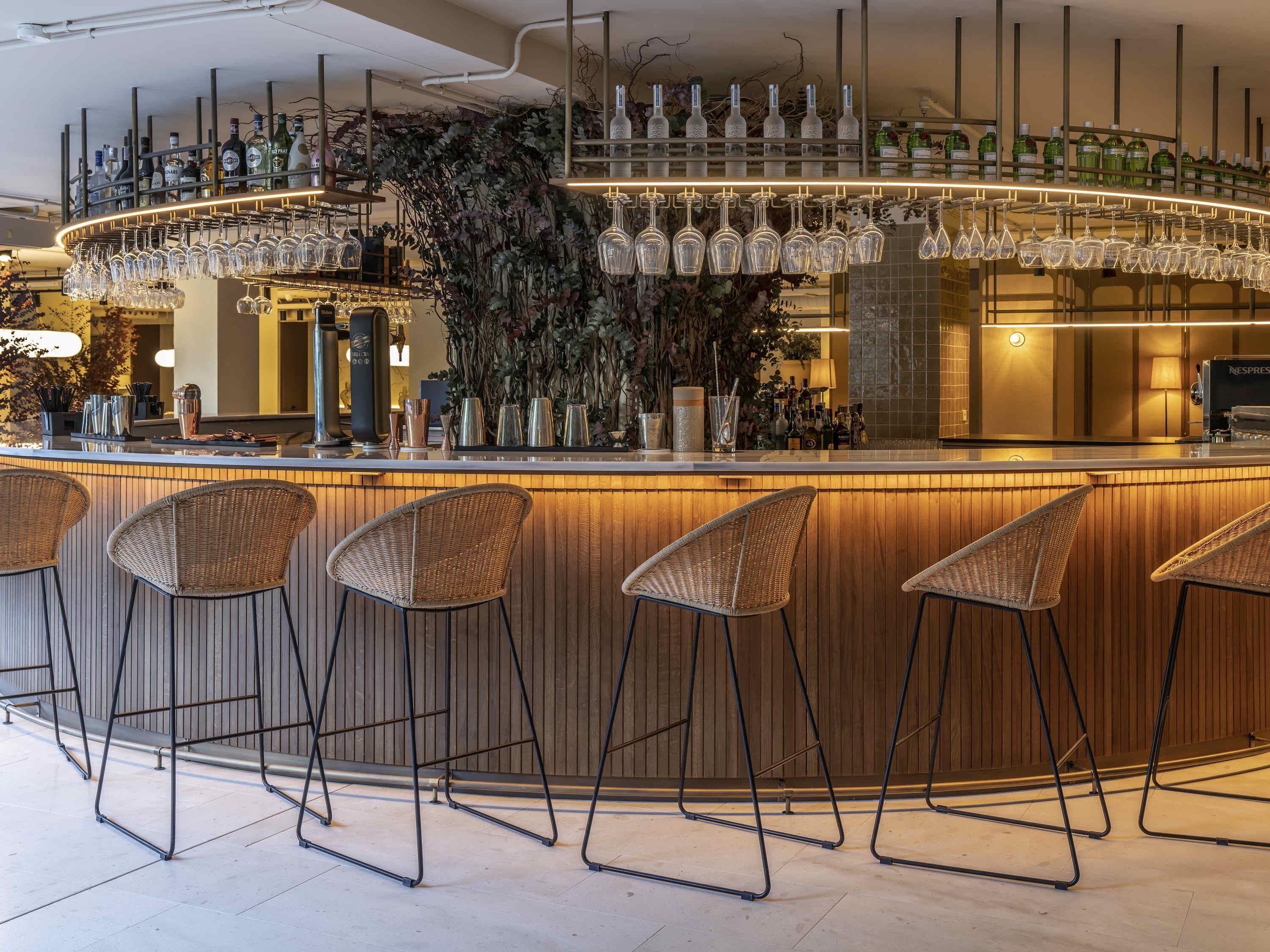 Uma área de bar com banquetas de vime, um balcão com máquina Nespresso e diversos frascos e copos.