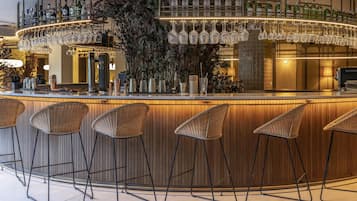 Uma área de bar com banquetas de vime, um balcão com máquina Nespresso e diversos frascos e copos.