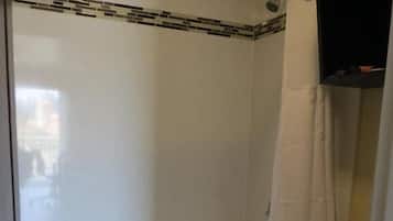 Casa de banho com chuveiro, sanita e parede revestida a azulejos.