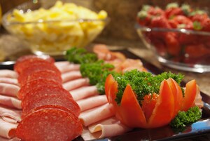 Um prato com fatias de carnes e vegetais, incluindo salame, presunto e um arranjo decorativo de tomate.