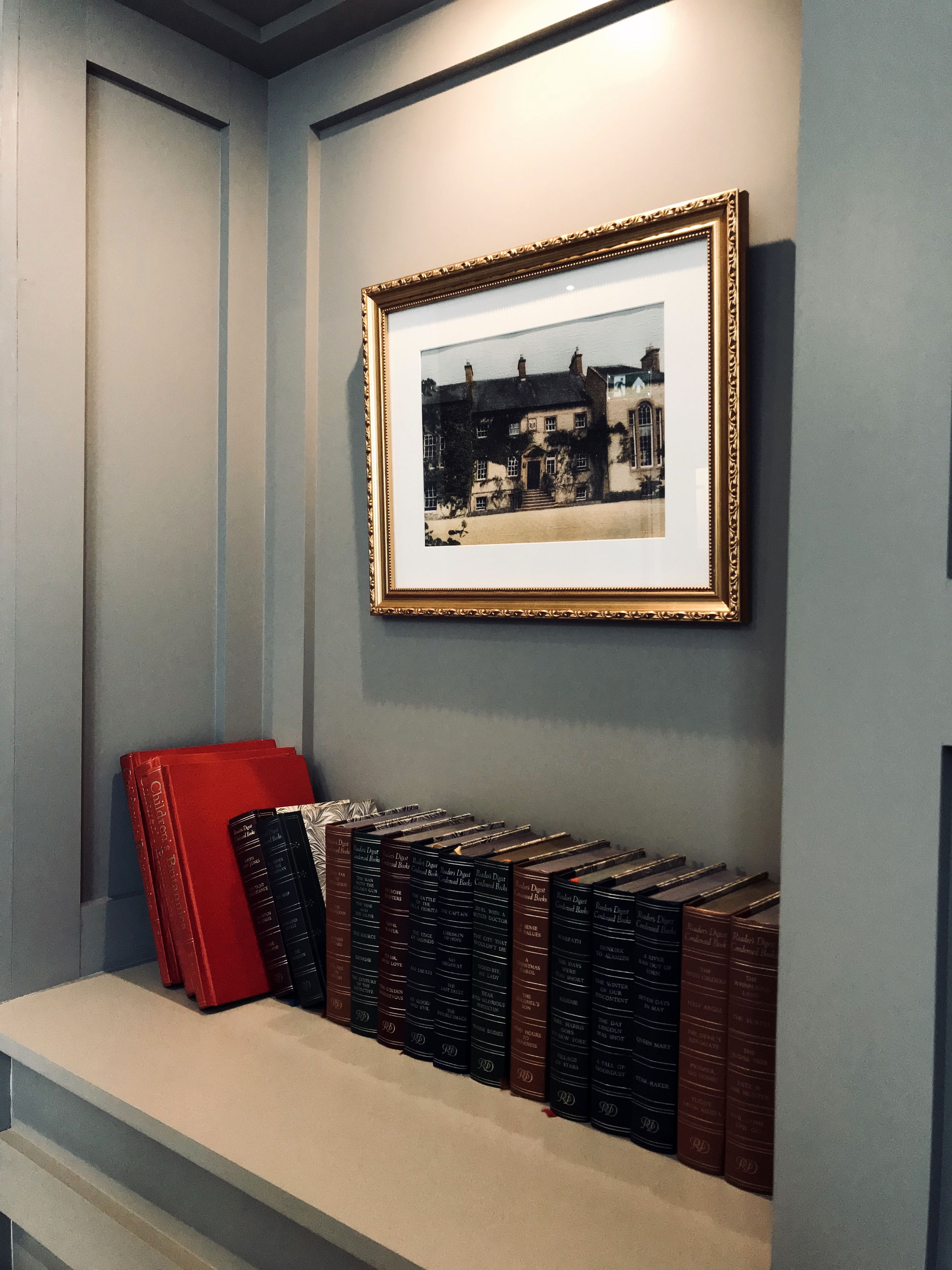 Uma estante com livros e uma fotografia emoldurada numa parede.