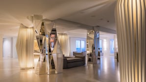 Um hall de hotel espaçoso e moderno, com luminárias geométricas, área de estar central e amplas janelas que proporcionam luz natural.