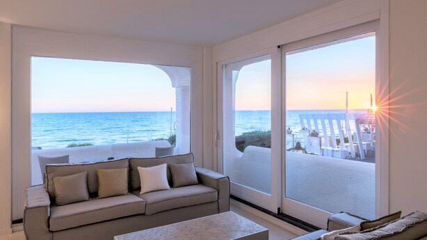 Sala de estar moderna com uma grande janela que dá para uma praia e um pôr do sol.