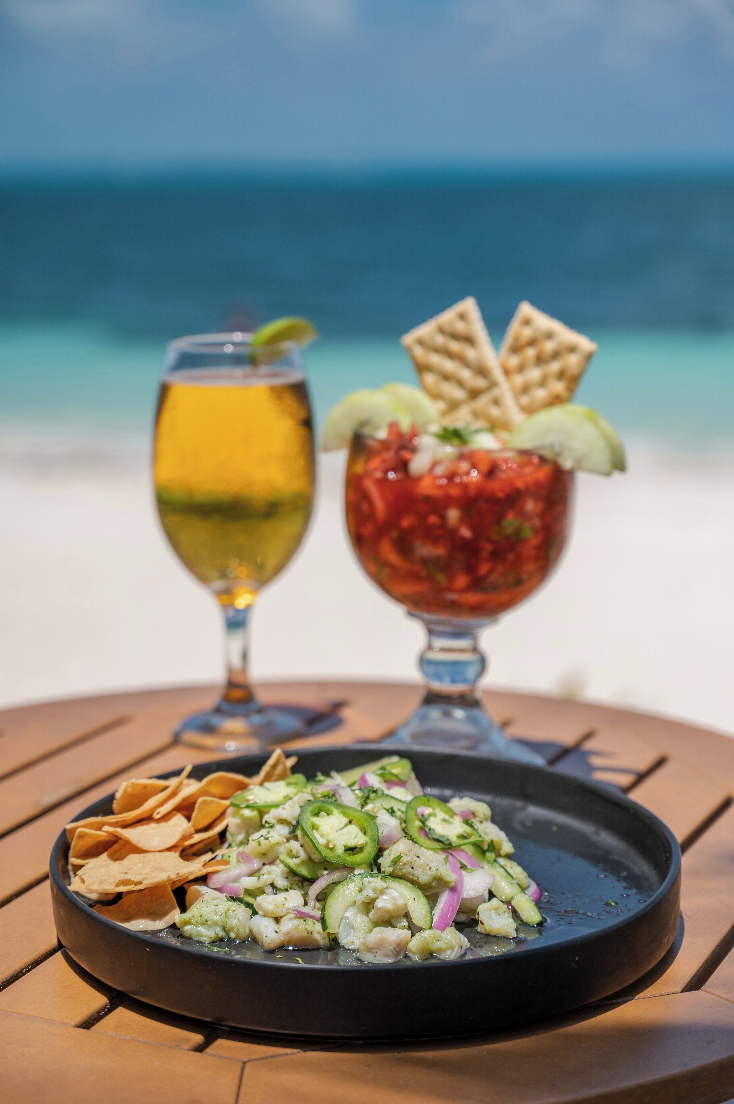 Prato de frutos do mar com batatas fritas e uma bebida sobre uma mesa na praia.