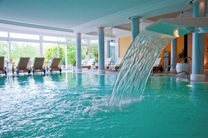 Piscina interna com cascata, espreguiçadeiras e amplas janelas.