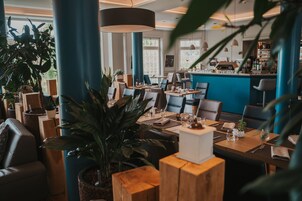 Um restaurante com mesas de madeira, cadeiras azuis e plantas em vasos.