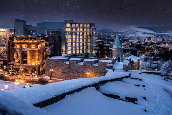Um edifício histórico com fachada de tijolos e decorações elaboradas, rodeado por ruas cobertas de neve e edifícios modernos.