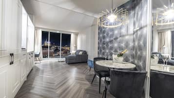 Uma sala de estar moderna com piso em padrão herringbone, um sofá cinzento, uma mesa redonda de mármore e uma parede estampada.